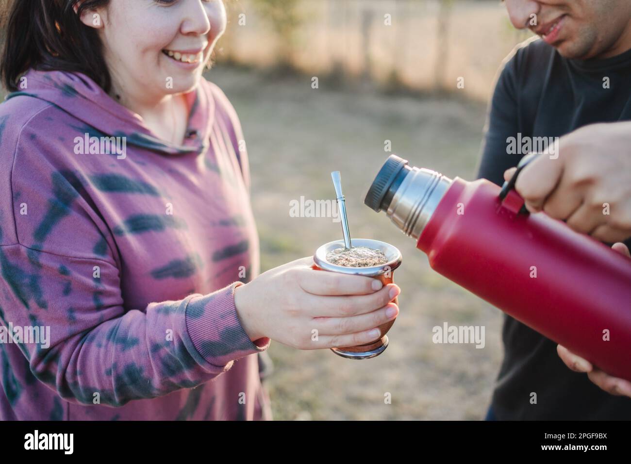Two smiling friends serving water with a thermos into yerba mate in the ...
