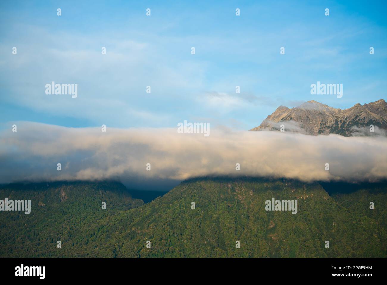 A majestic mountain range illuminated by the sun, with light clouds scattered across the ...