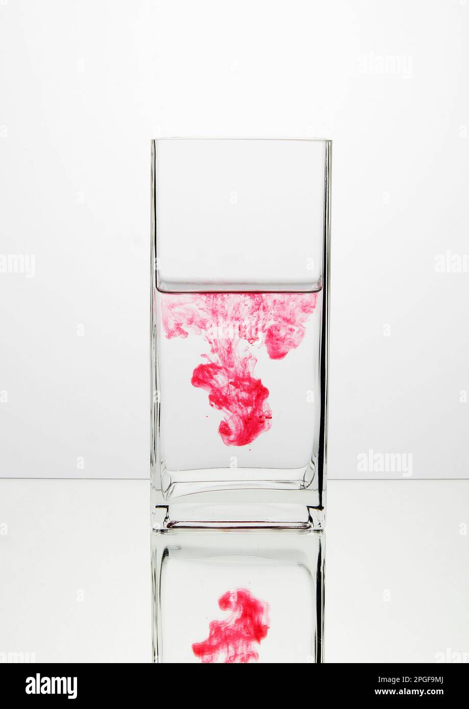 A crystal-clear glass of water with a vibrant pink droplet suspended in ...
