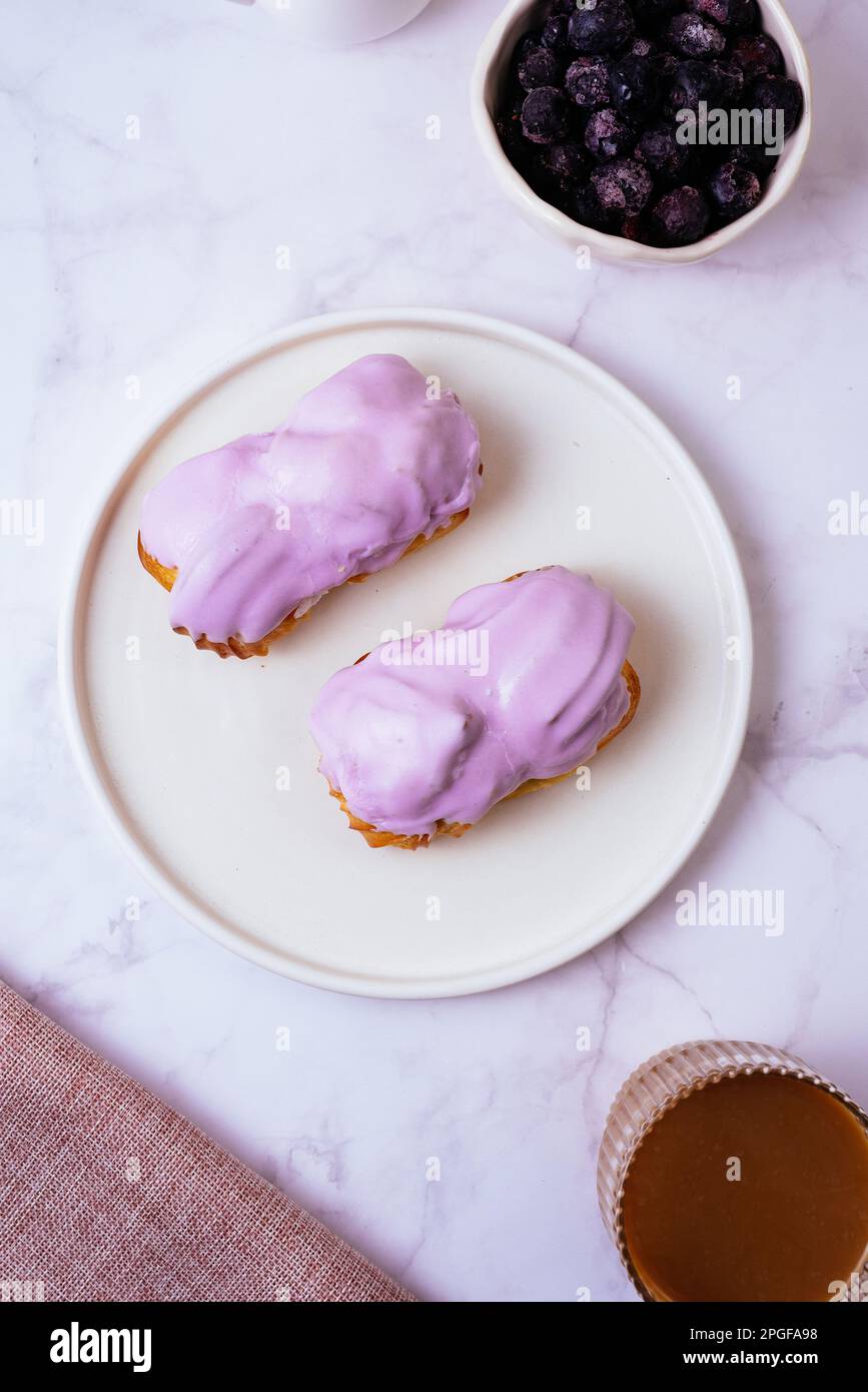 eclair in purple berry glaze and coffee with milk in a glass Stock ...