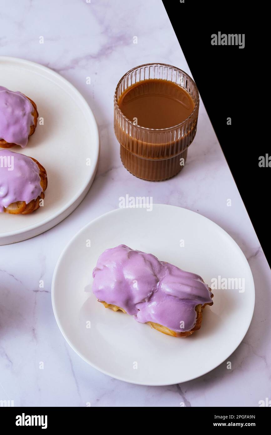 eclair in purple berry glaze and coffee with milk in a glass Stock ...