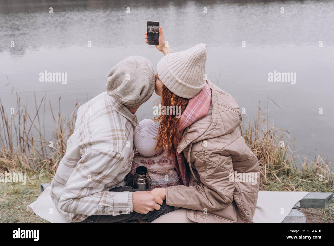 A family with a small child is resting by the river in cold weather ...