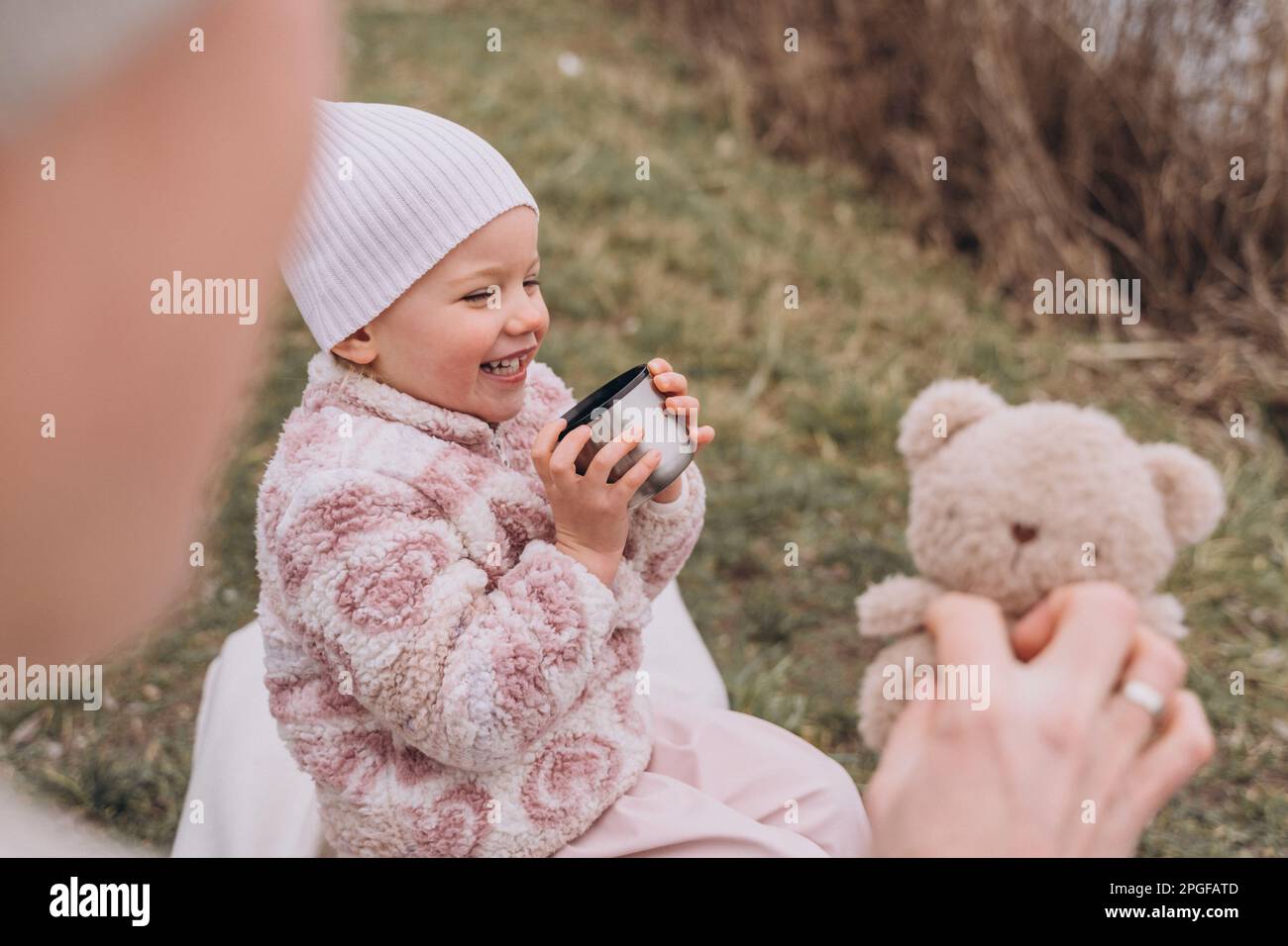 Toothless baby girl in the park laughs and drinks tea from the thermos ...