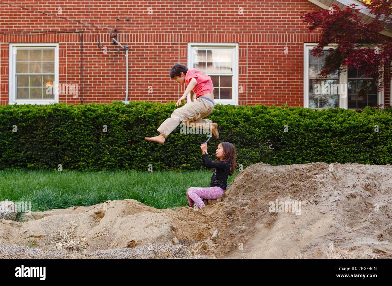 A girl with phone films brother leaping over her head in sandpit Stock ...