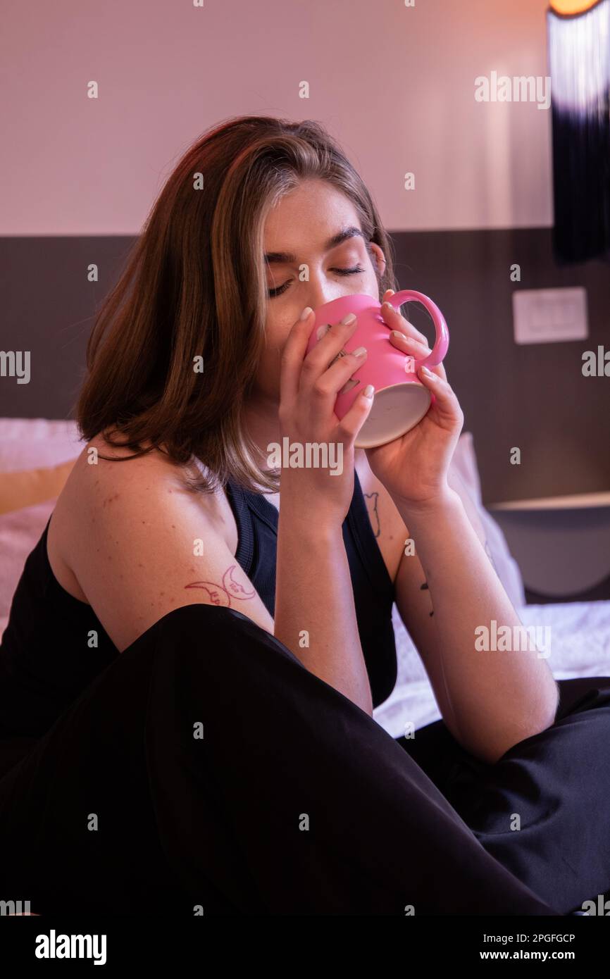 Woman Sits On Bed With Coffee in Hand Taking a Sip Stock Photo - Alamy