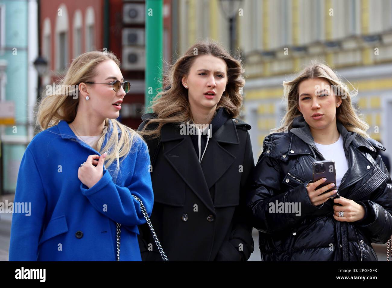 Three girlfriends in coats walking on a street. Pretty stylish girls in ...