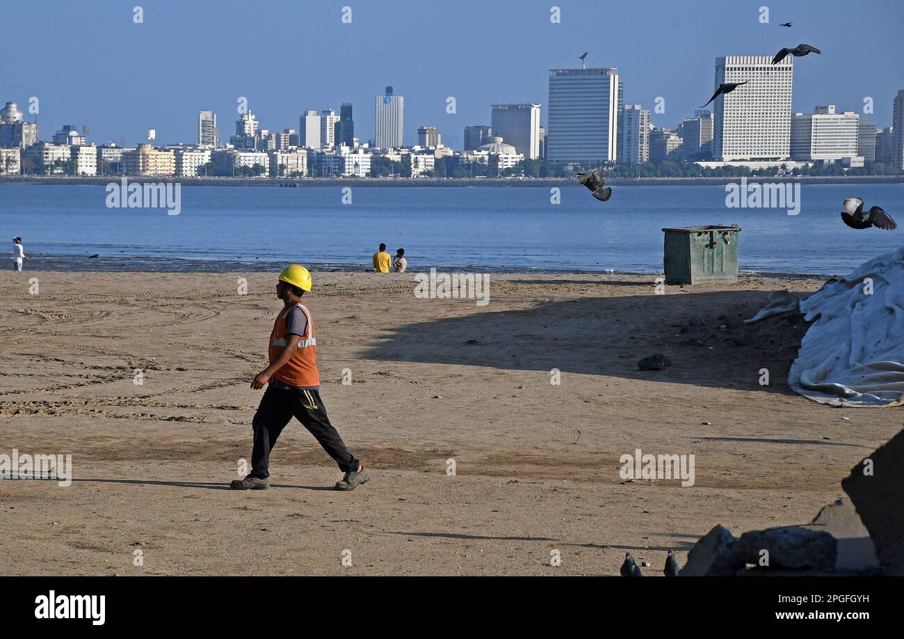 Mumbai, India. 21st Mar, 2023. A labourer walks along the beach as the ...