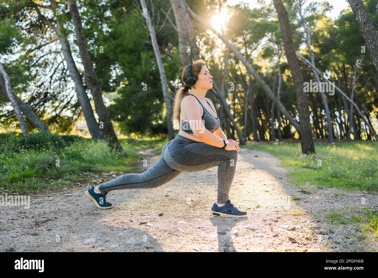 Adorable fat woman in tracksuit is engaged in fitness outdoor side view ...