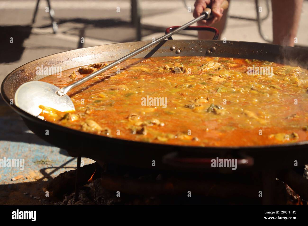 A street traditional cooking with a large stainless steel frying pan in ...