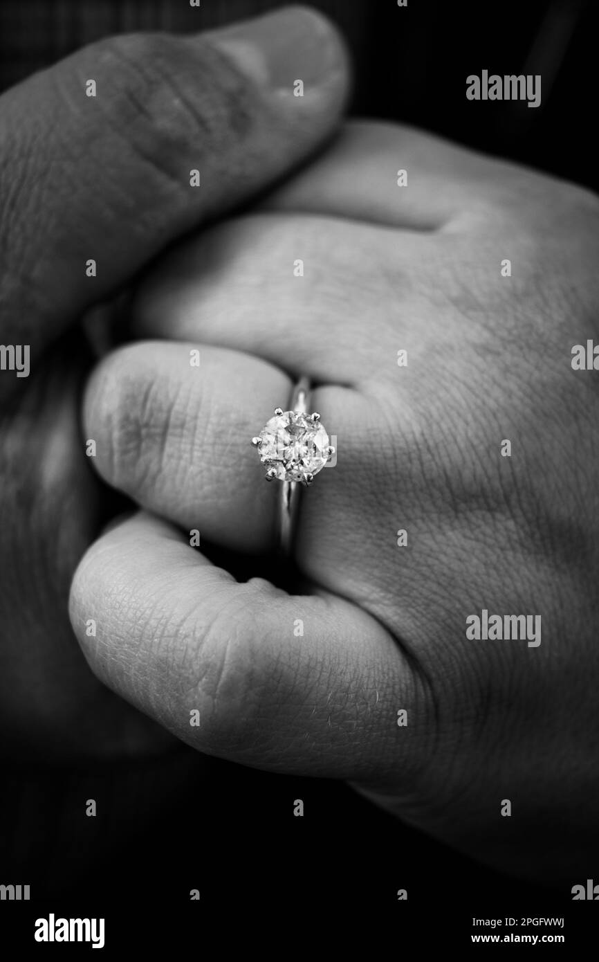 A vertical greyscale of a man holding his wife's hand with her wedding ...