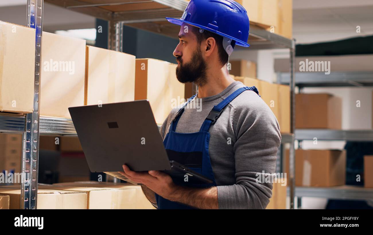 Depot supervisor holding laptop with stock logistics list, looking at ...