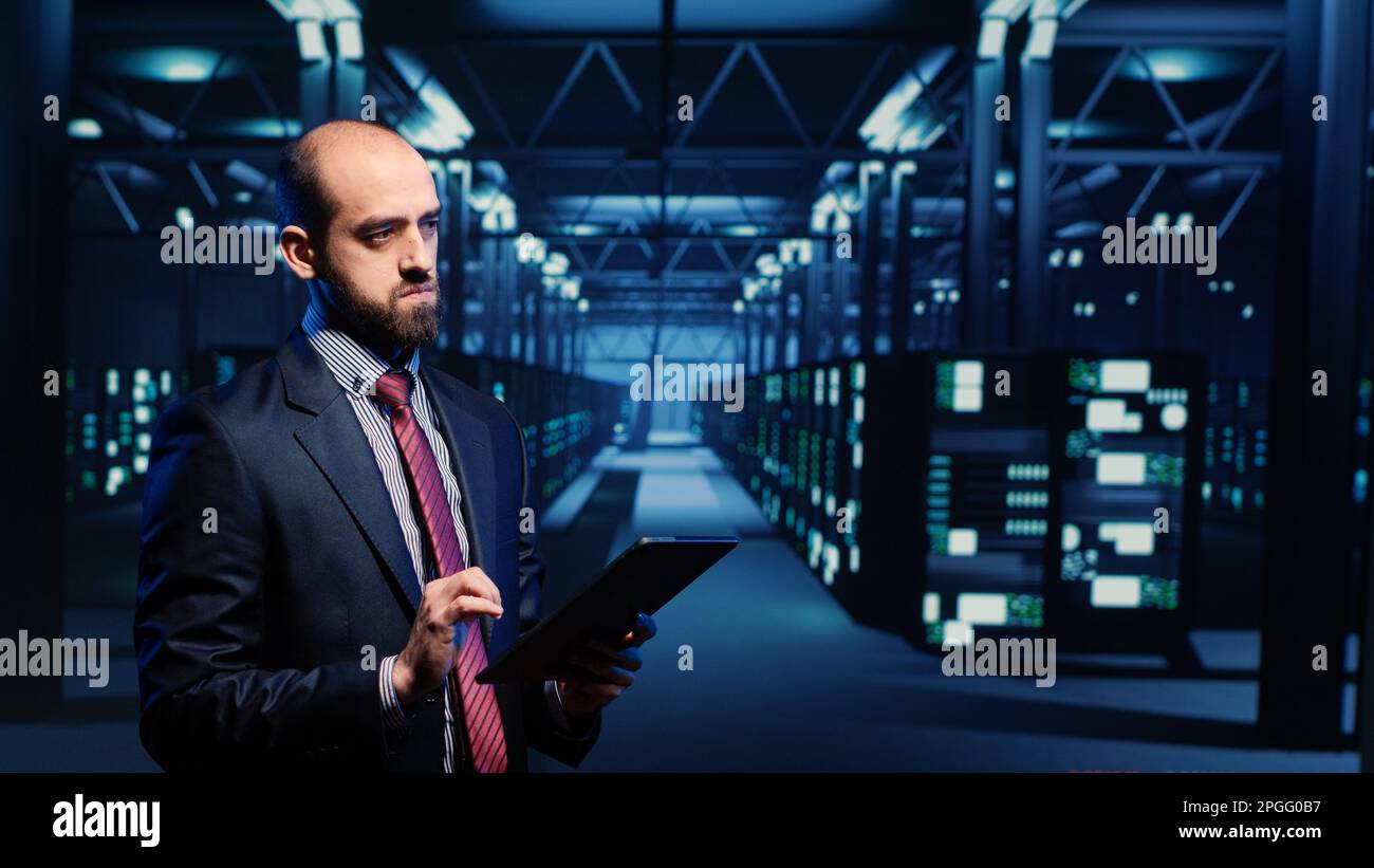 IT engineer using tablet in high tech server room, planning networking computer system. Database ...
