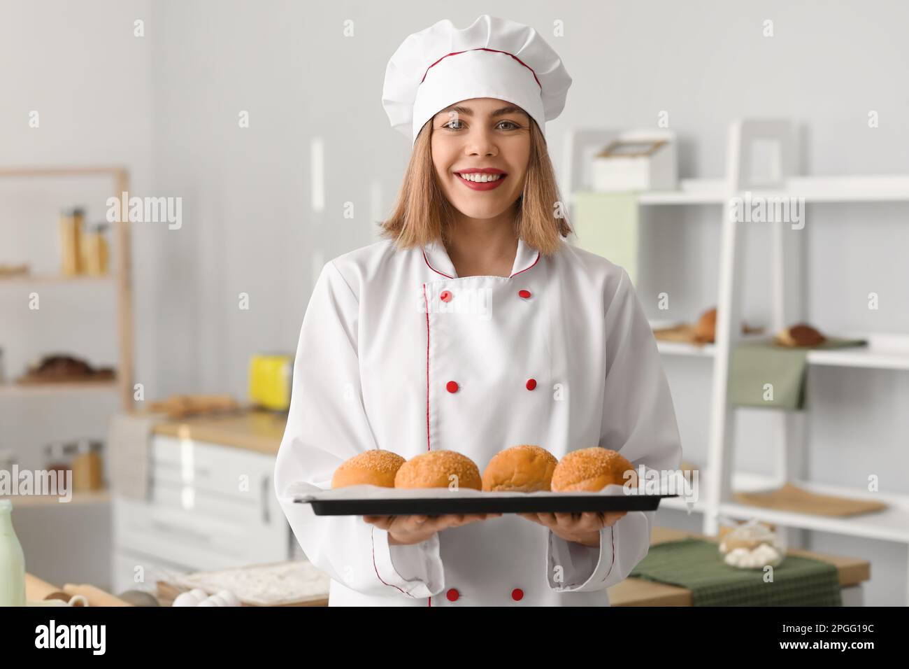 Female baker with tray of tasty buns in kitchen Stock Photo - Alamy