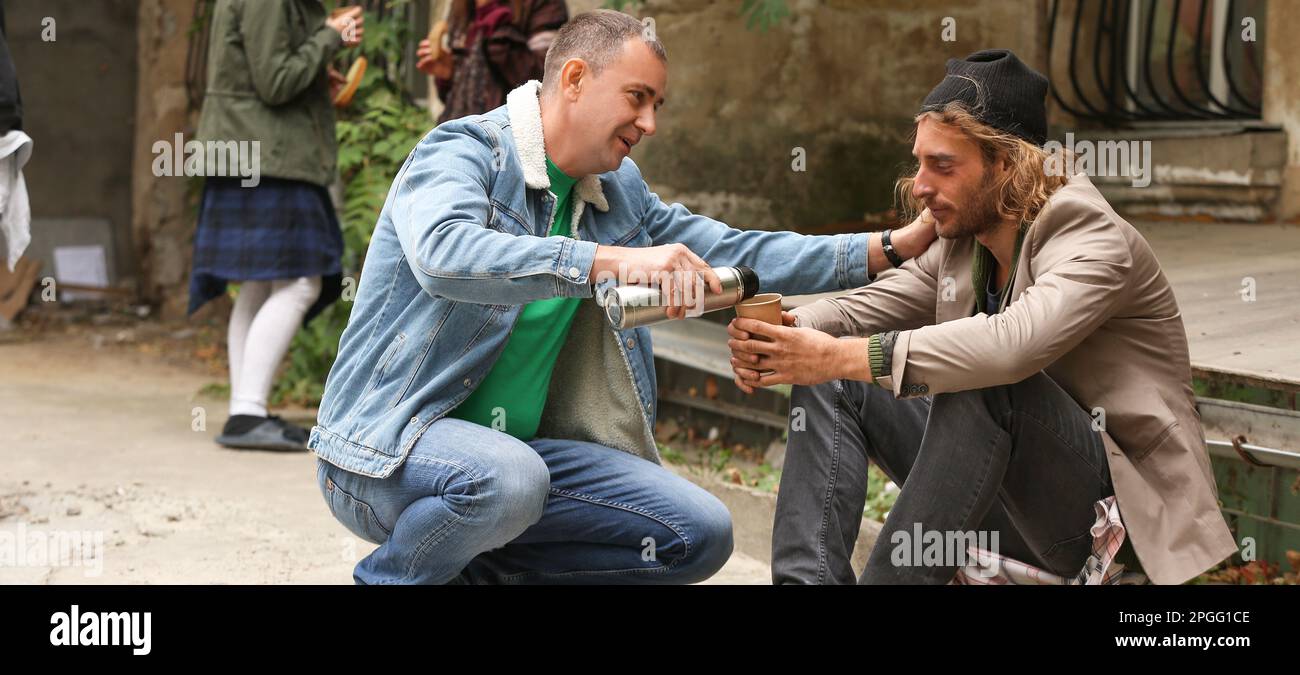 Volunteer giving drink to homeless man outdoors Stock Photo - Alamy