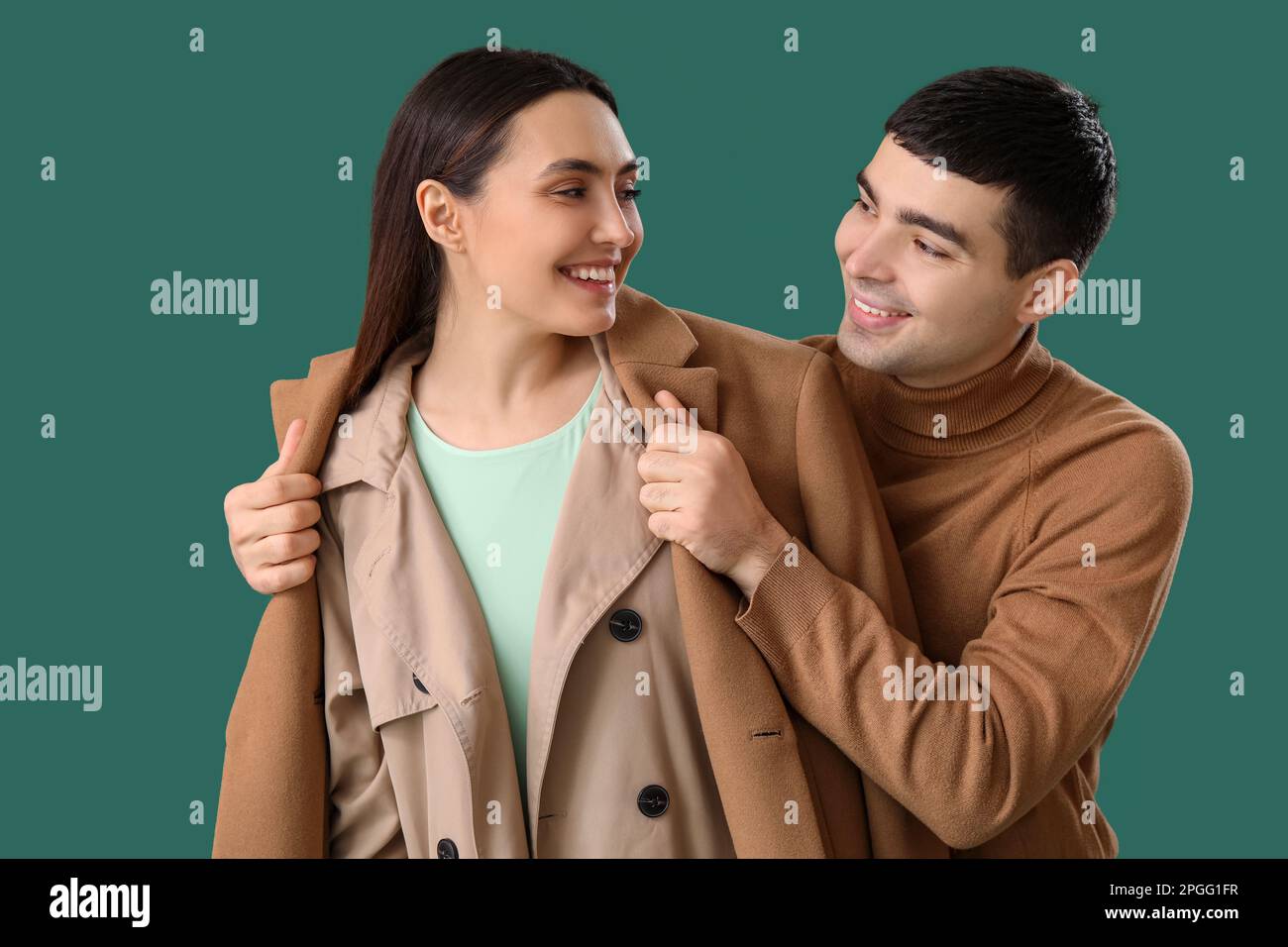 Young man putting coat onto his girlfriend on green background Stock ...