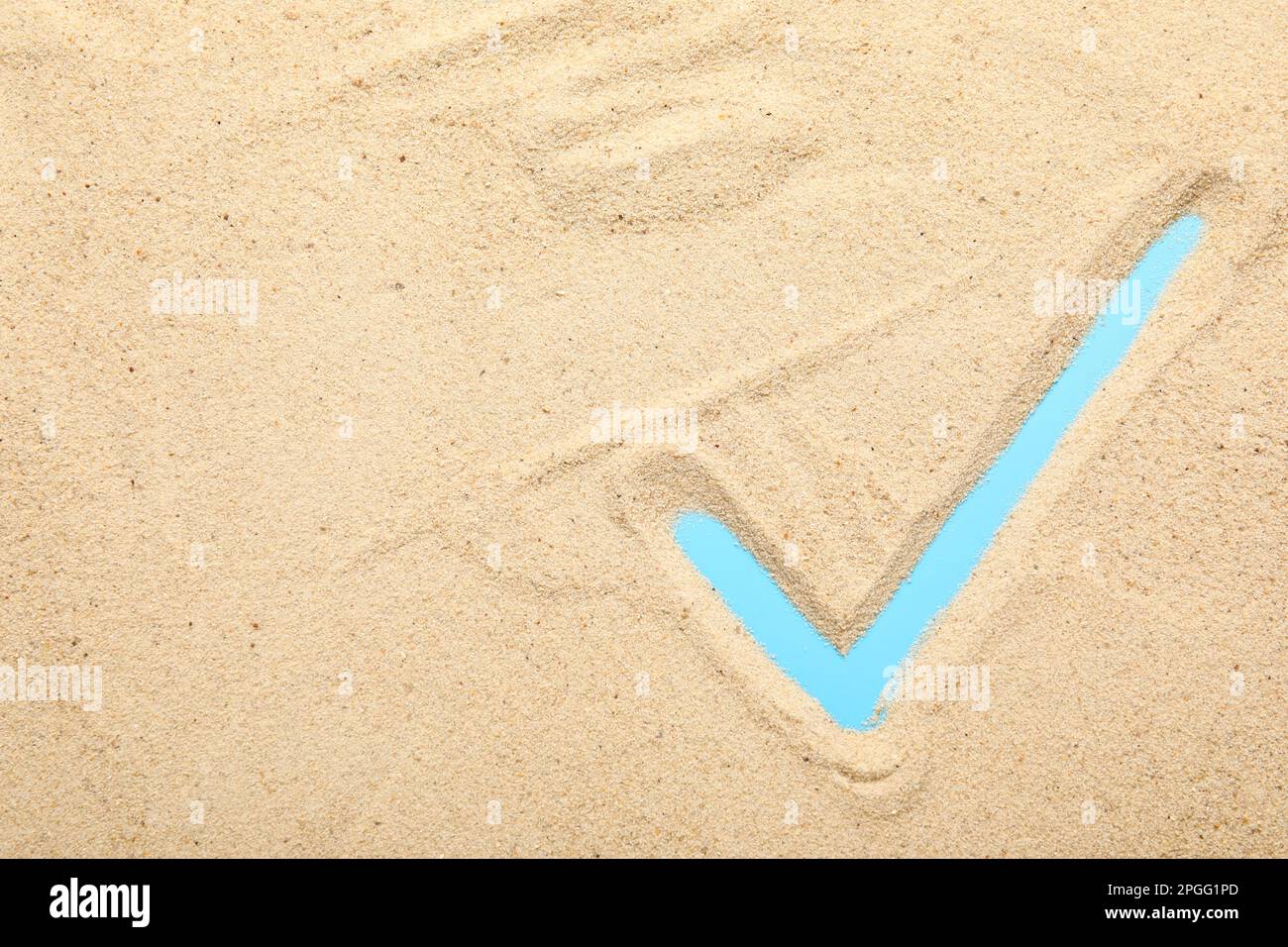 Check mark made of sand on blue background Stock Photo - Alamy