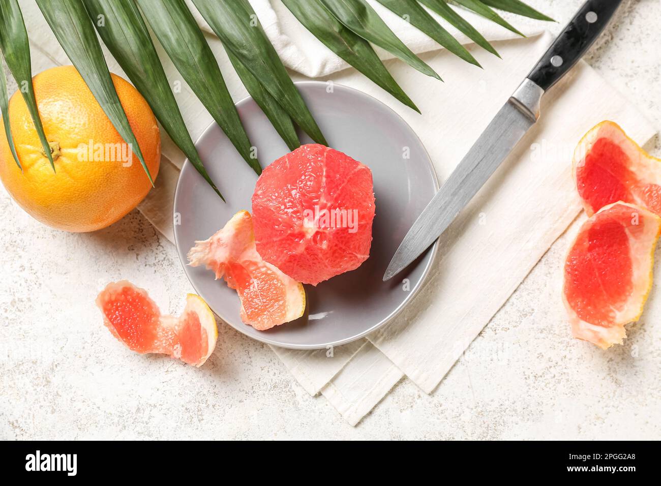 Plate with peeled grapefruit, knife and palm leaf on light background ...