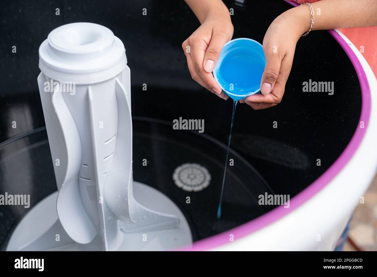 A young woman is pouring some liquid detergent into a top load washing ...
