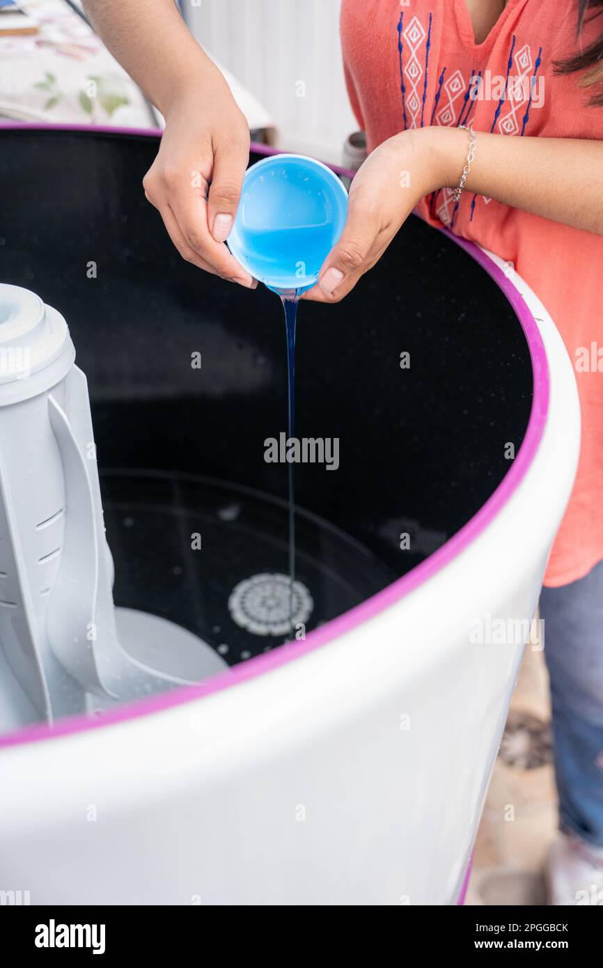 A young woman is pouring some liquid detergent into a top load washing ...