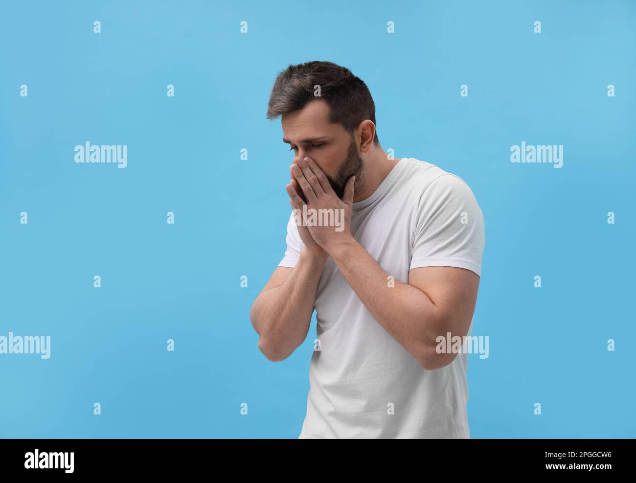 Man sneezing on light blue background. Cold symptoms Stock Photo - Alamy