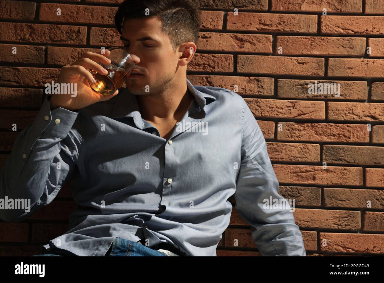 Addicted man drinking alcohol near red brick wall Stock Photo - Alamy