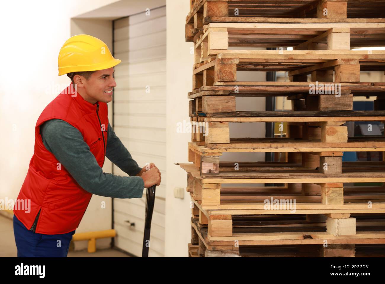 Worker moving wooden pallets with manual forklift in warehouse Stock ...
