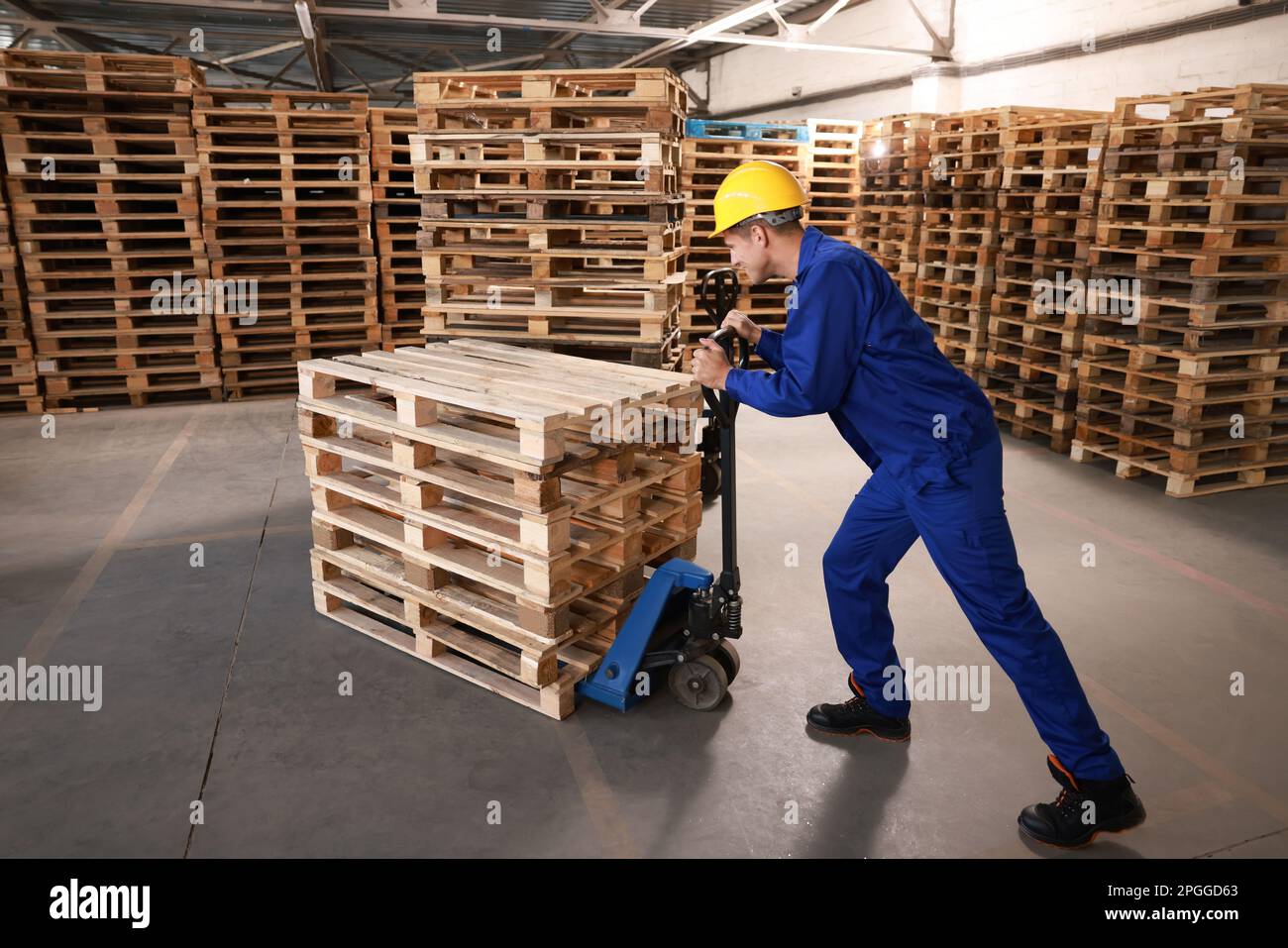 Worker moving wooden pallets with manual forklift in warehouse Stock ...