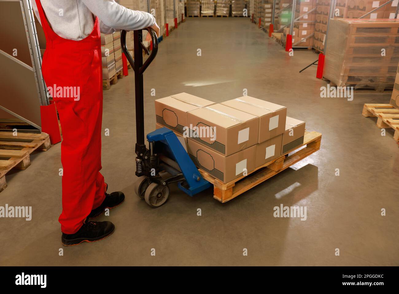 Worker moving cardboard boxes with manual forklift in warehouse ...