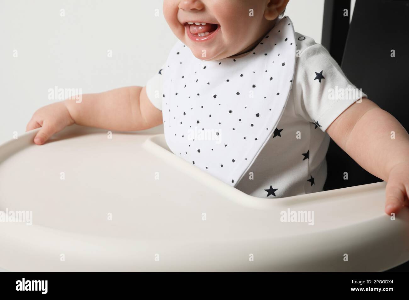 Cute little baby wearing bib in highchair on white background, closeup ...