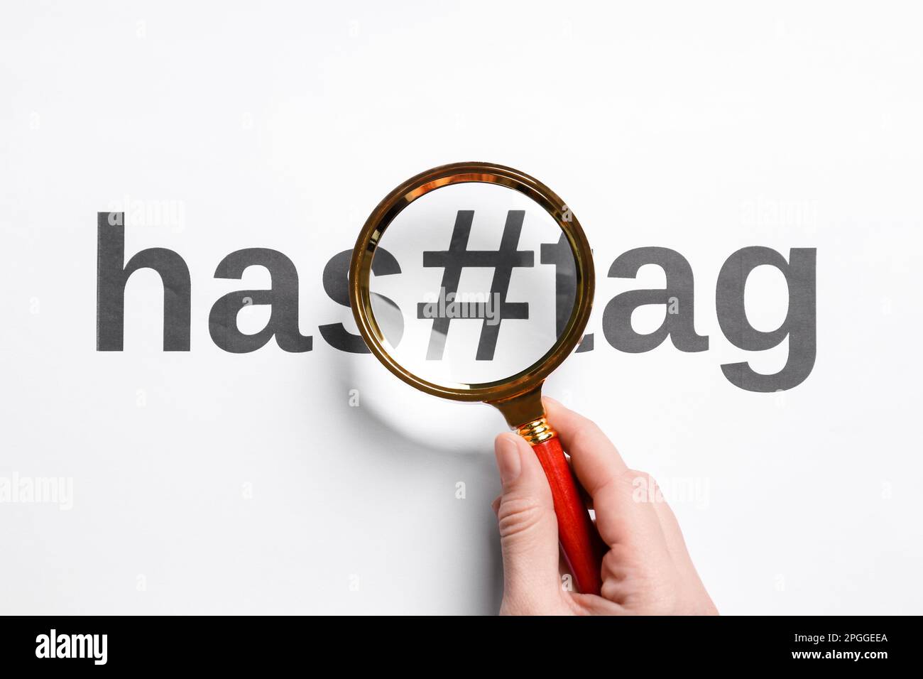 Woman holding magnifying glass over word Hashtag with symbol on white ...