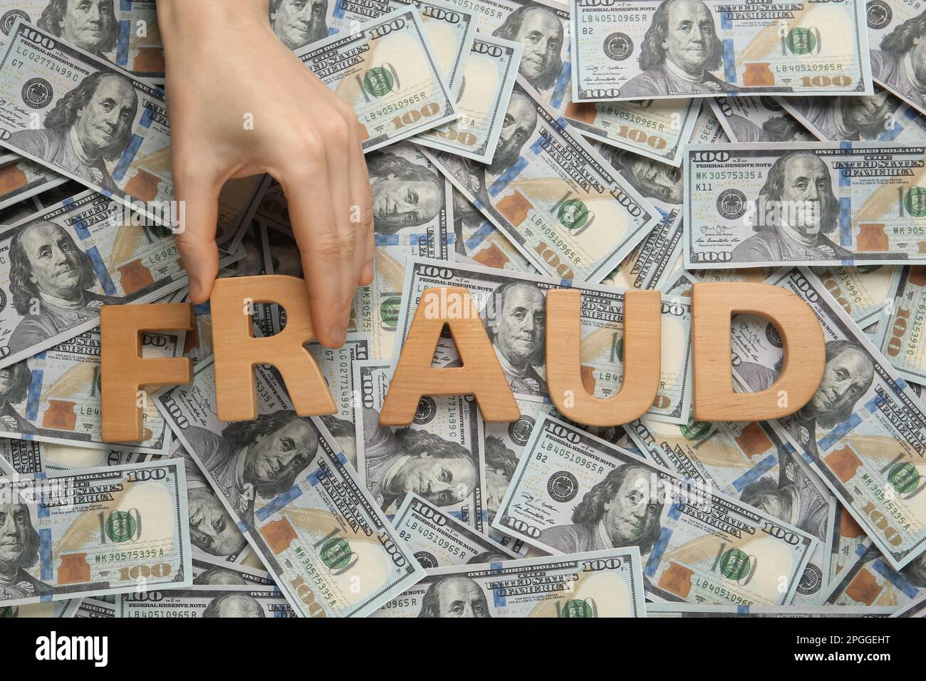 Woman making word Fraud with wooden letters on pile of dollar banknotes ...