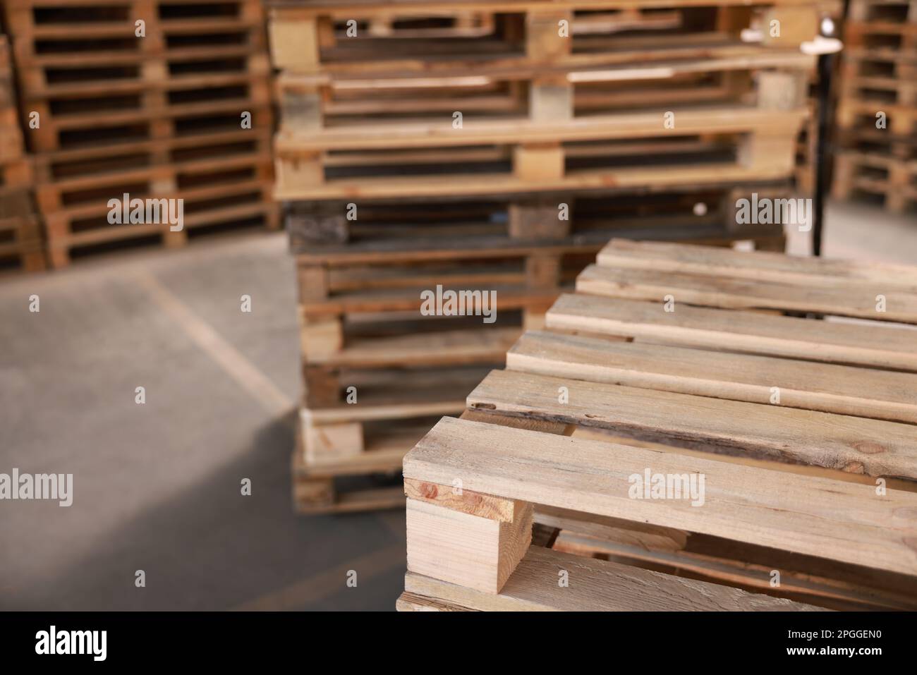 Many empty wooden pallets stacked in warehouse, closeup. Space for text ...