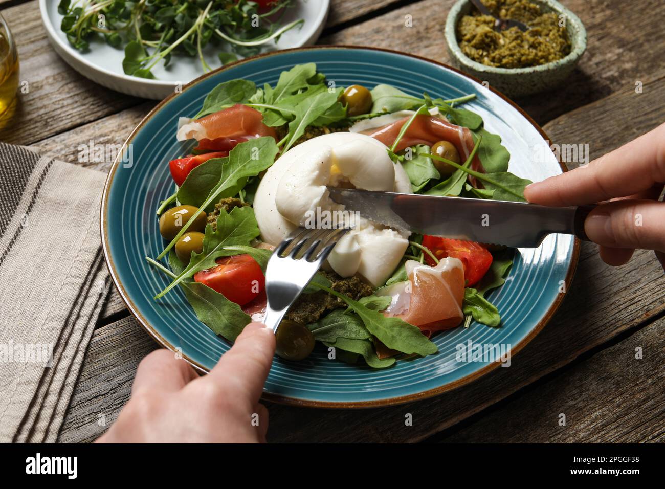 Woman eating delicious burrata salad at wooden table, closeup Stock ...