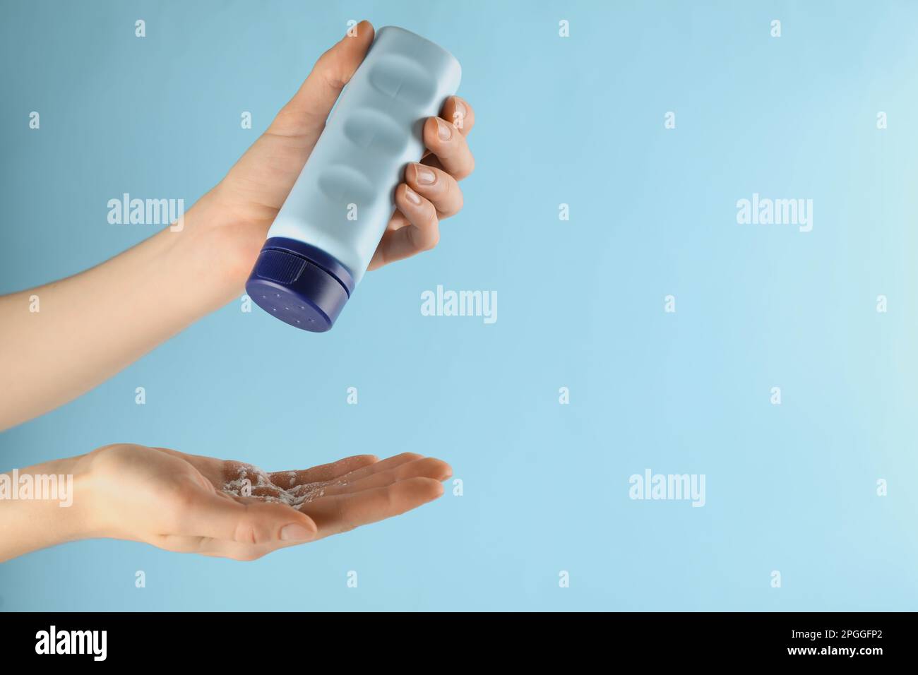 Woman applying dusting powder on light blue background, closeup. Space ...