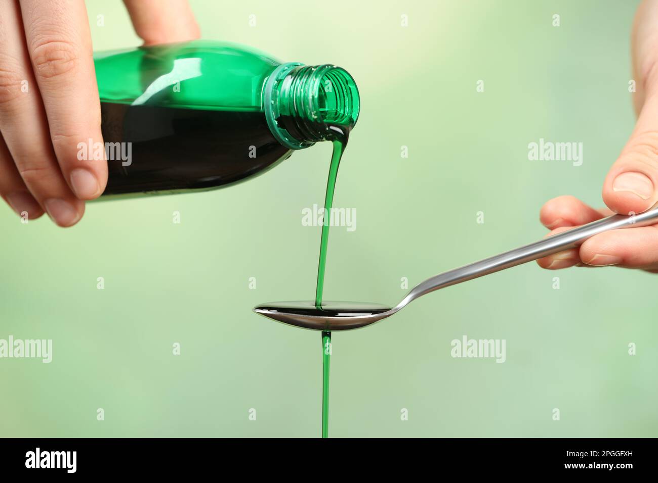Woman pouring cough syrup into spoon on light green background, closeup ...