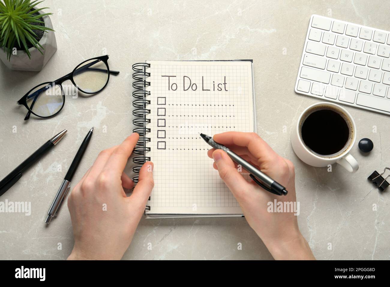 Woman filling To Do list in notepad at light grey marble table, top ...