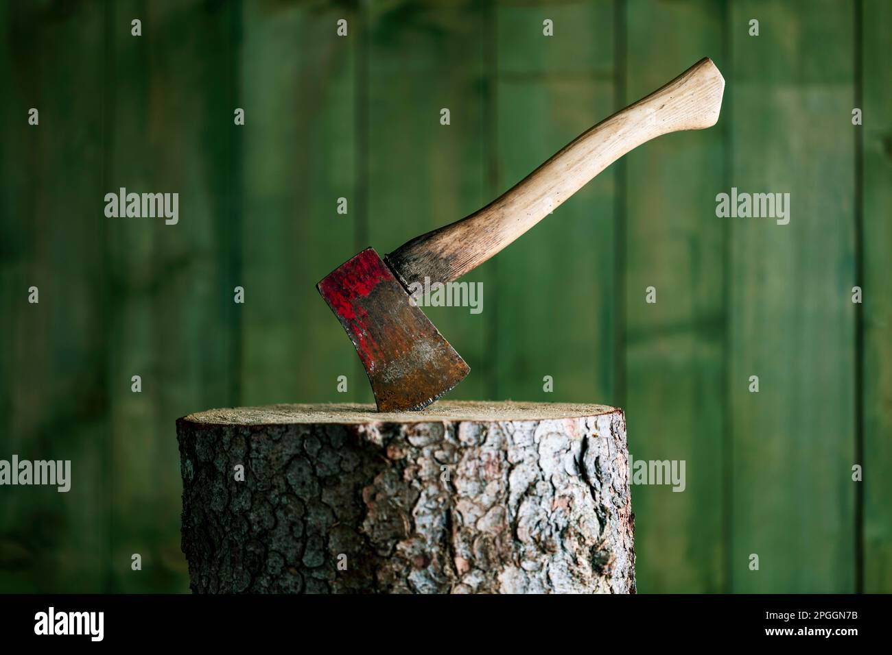 An axe on a chopping block in front of a green wooden wall, studio shot ...