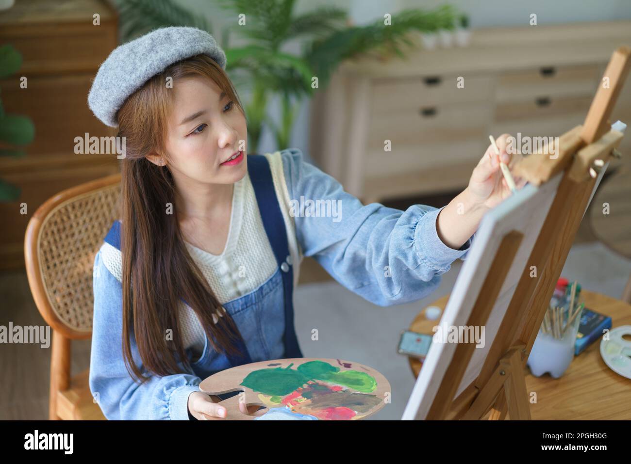 Young female painter holds color palette and use brush to painting ...