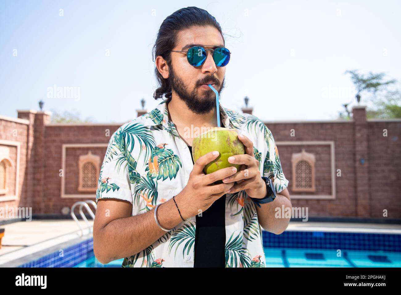 Young thirsty Indian man wearing sunglasses and casual cloths drinking ...