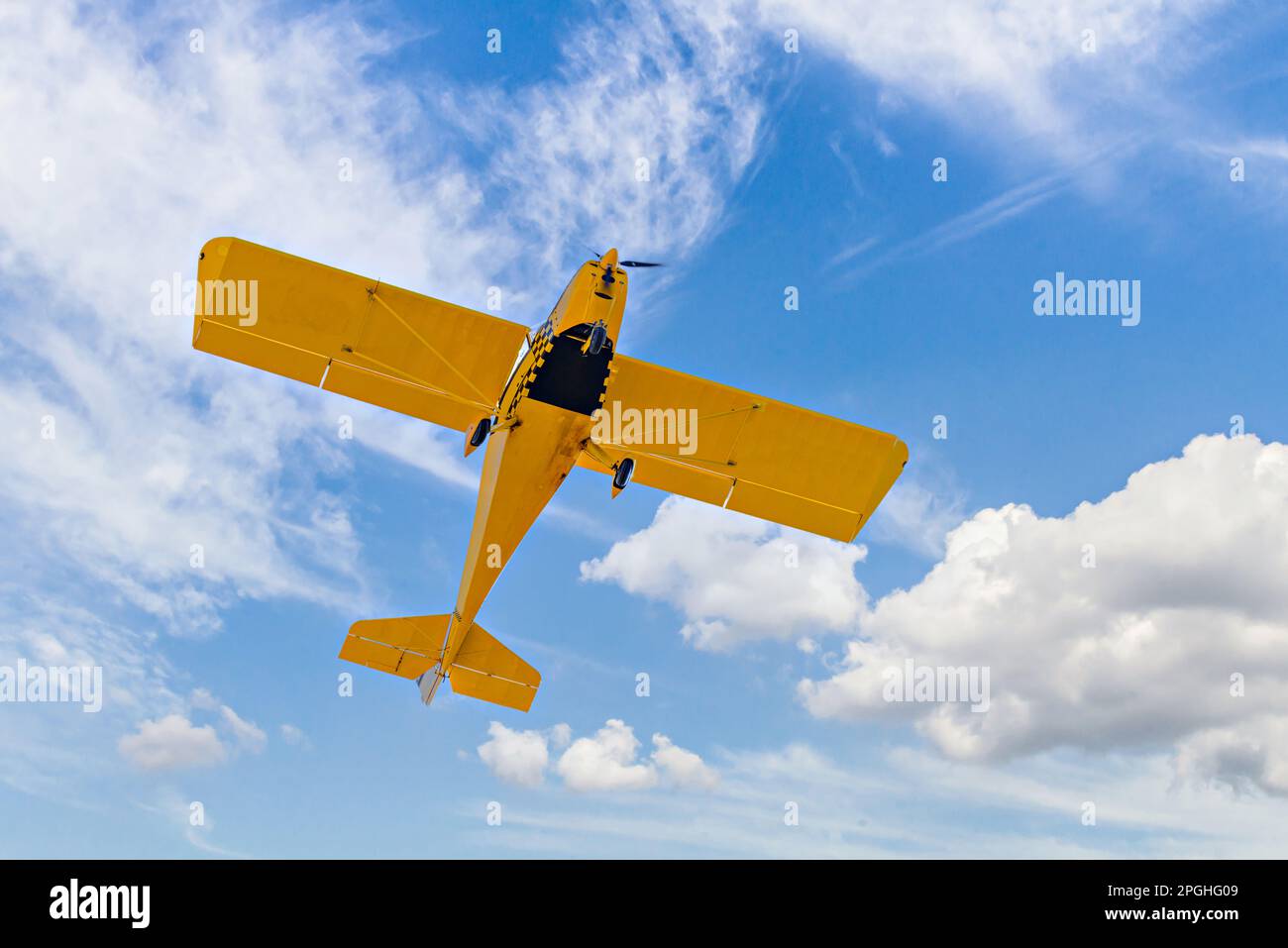 Yellow single-engine ultralight airplane flying in the blue sky with ...