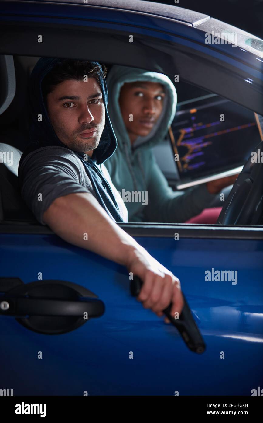 Hacking is a crime. two armed young hackers using a laptop in a car ...