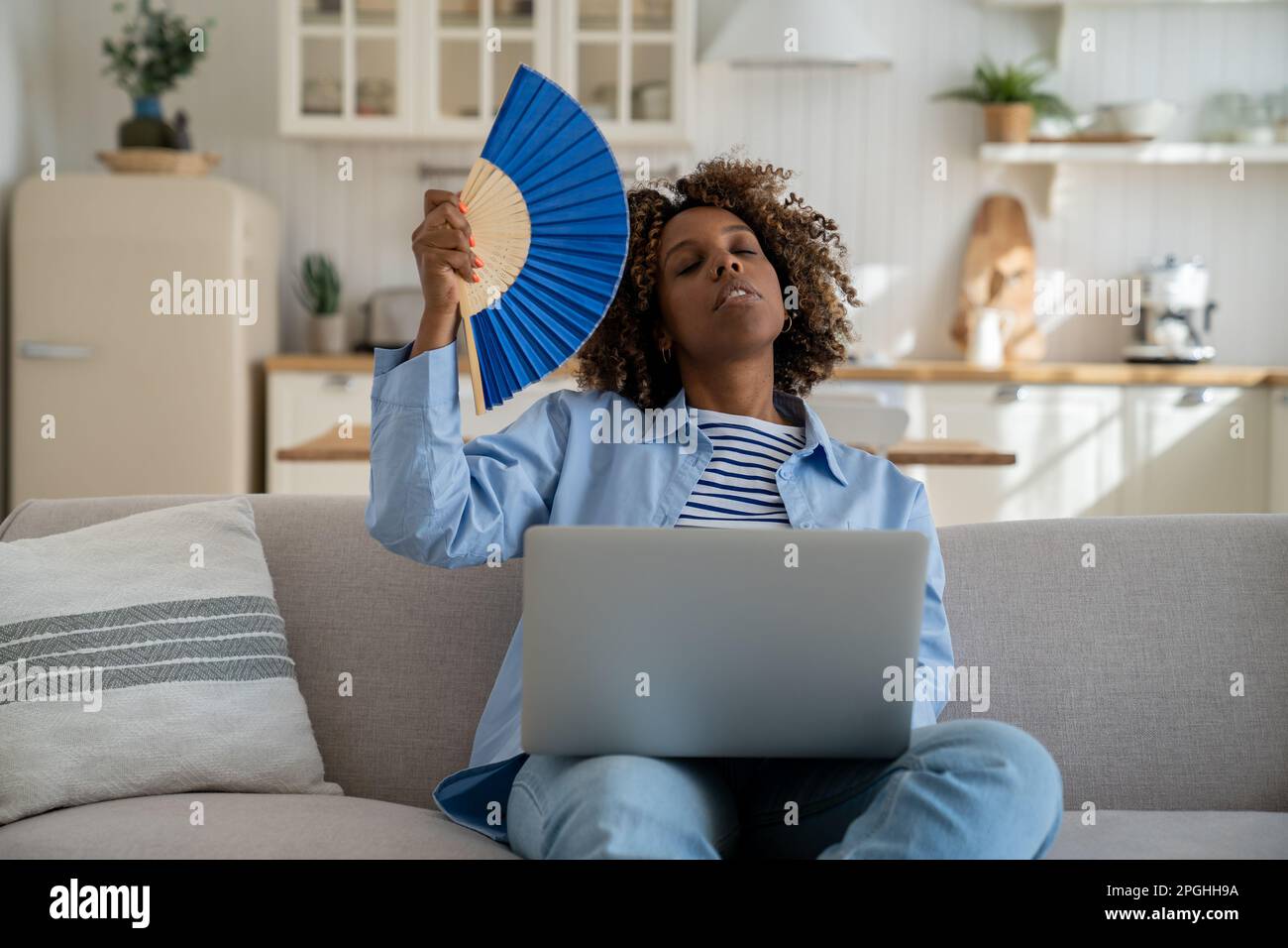 Tired mixed race woman waving fan in hand suffer from heat day while ...