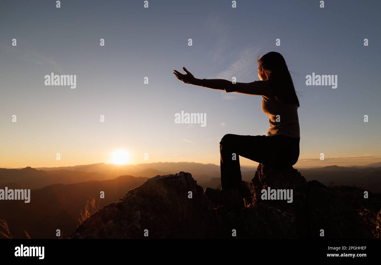 Silhouette of man rise hand up on top of mountain and sunset sky ...