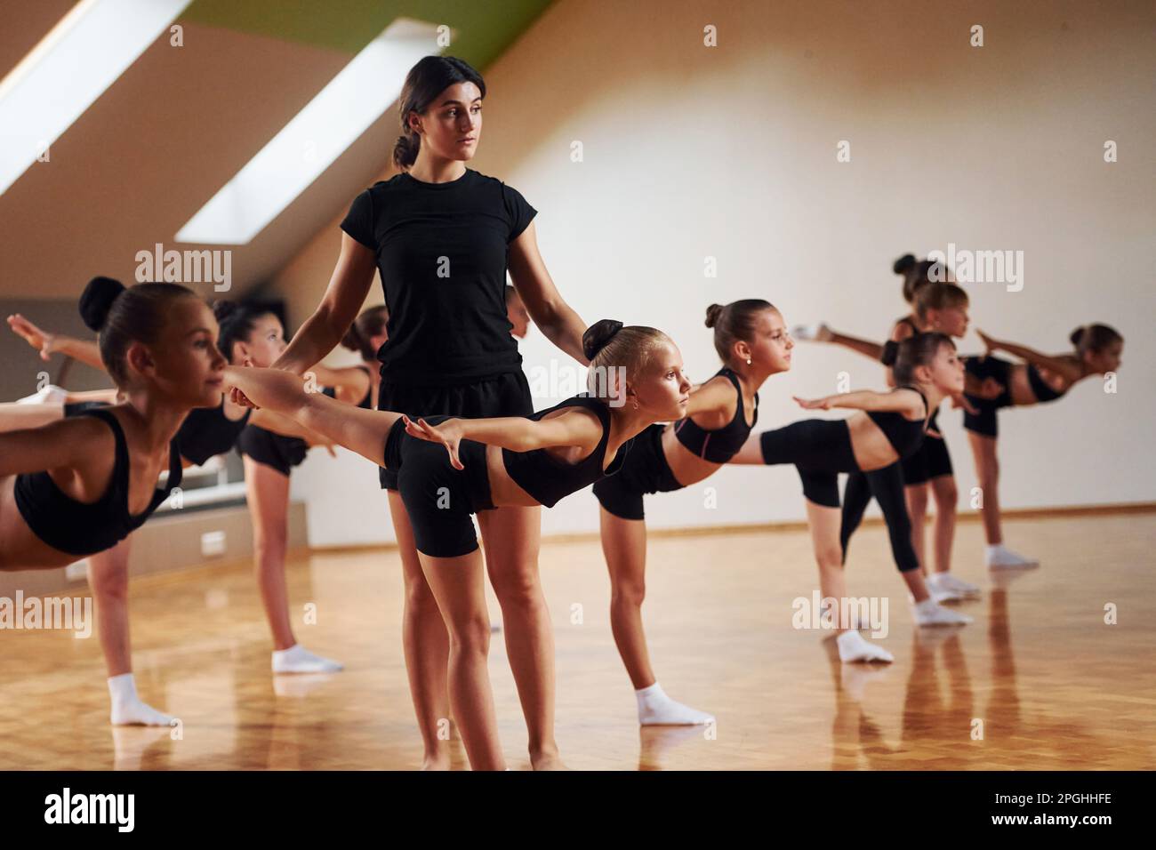 Coach is helping. Group of female kids practicing athletic exercises ...