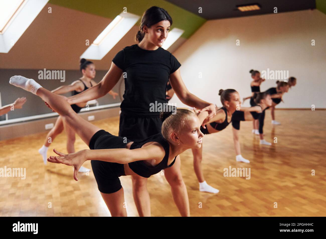 Coach is helping. Group of female kids practicing athletic exercises ...