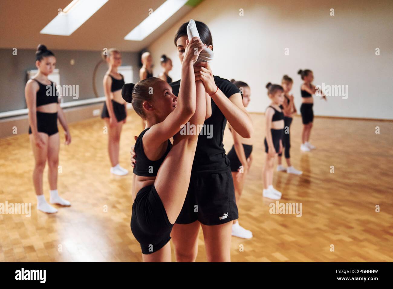 Coach is helping. Group of female kids practicing athletic exercises ...