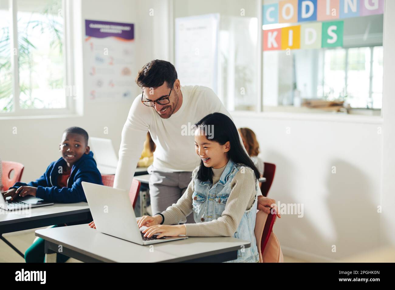 Teacher guiding a child with coding on a laptop in a computer academy. In a classroom that ...
