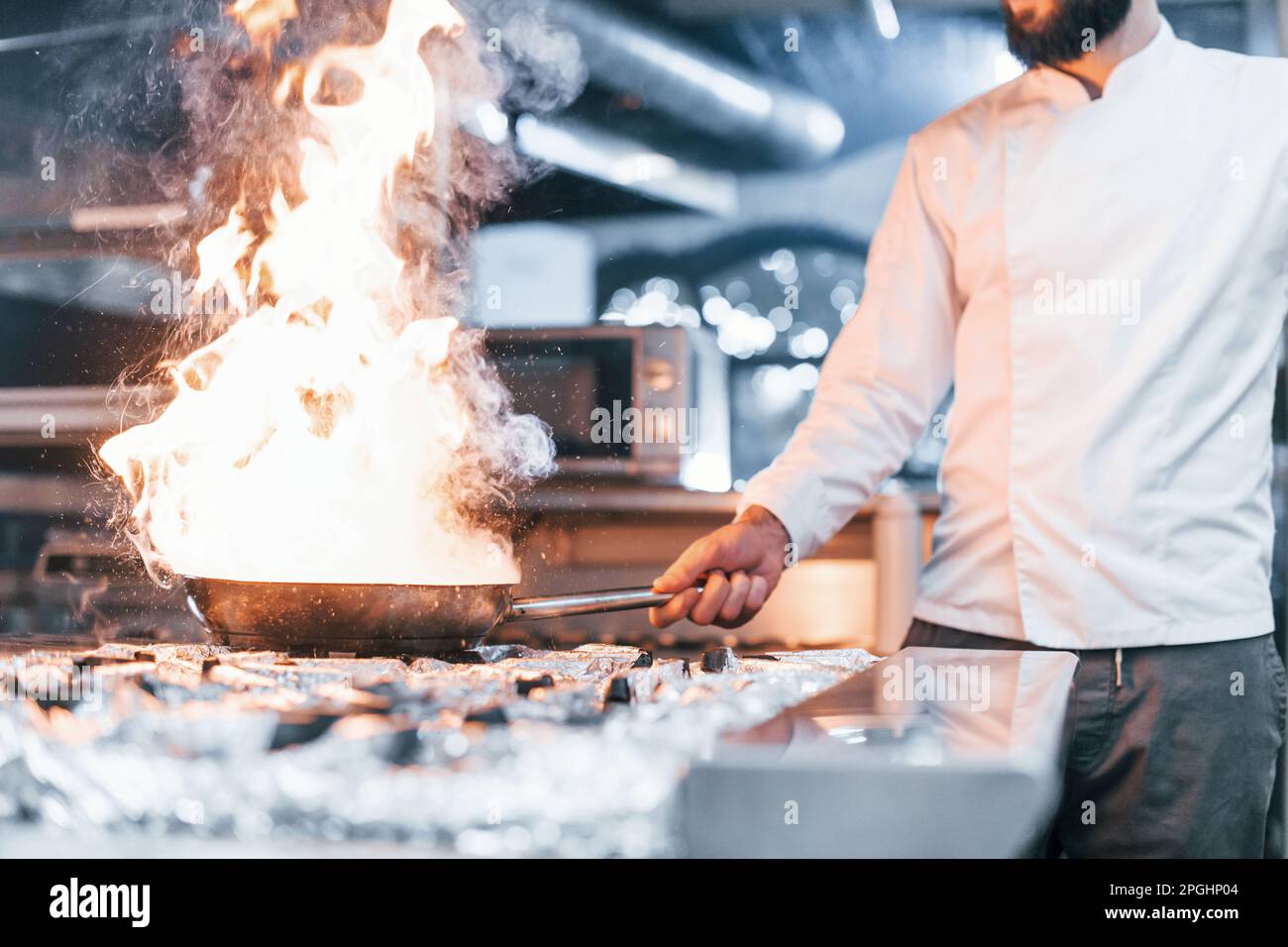 Frying pan is on fire. Chef in white uniform cooking food at kitchen ...