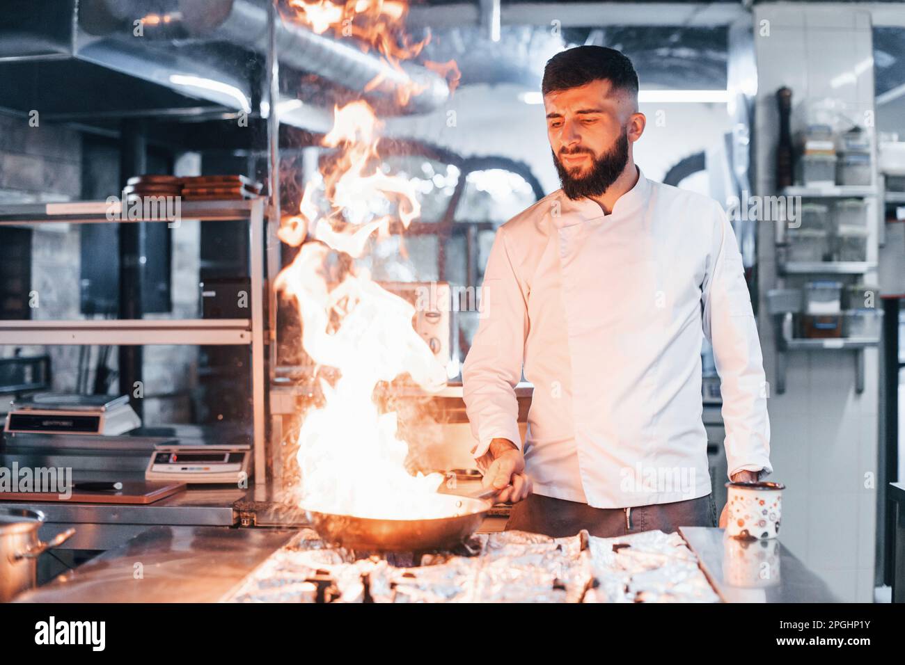 Frying pan is on fire. Chef in white uniform cooking food at kitchen ...