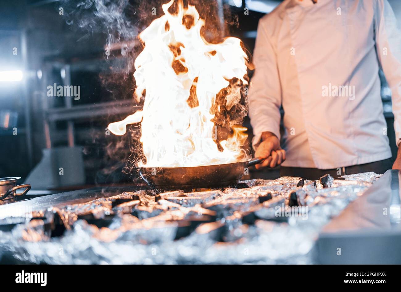 Frying pan is on fire. Chef in white uniform cooking food at kitchen ...